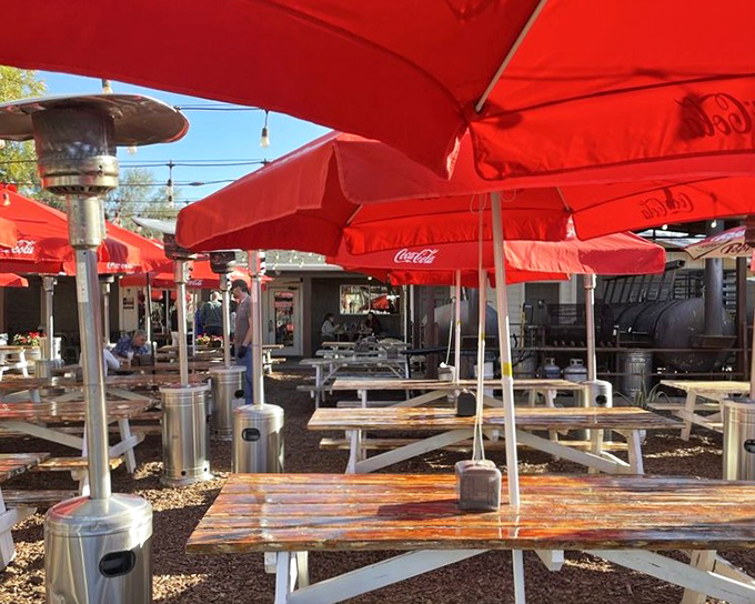 Red umbrellas provide shade for serious barbecue contemplation. Even in the desert heat, some pleasures are worth braving the elements.