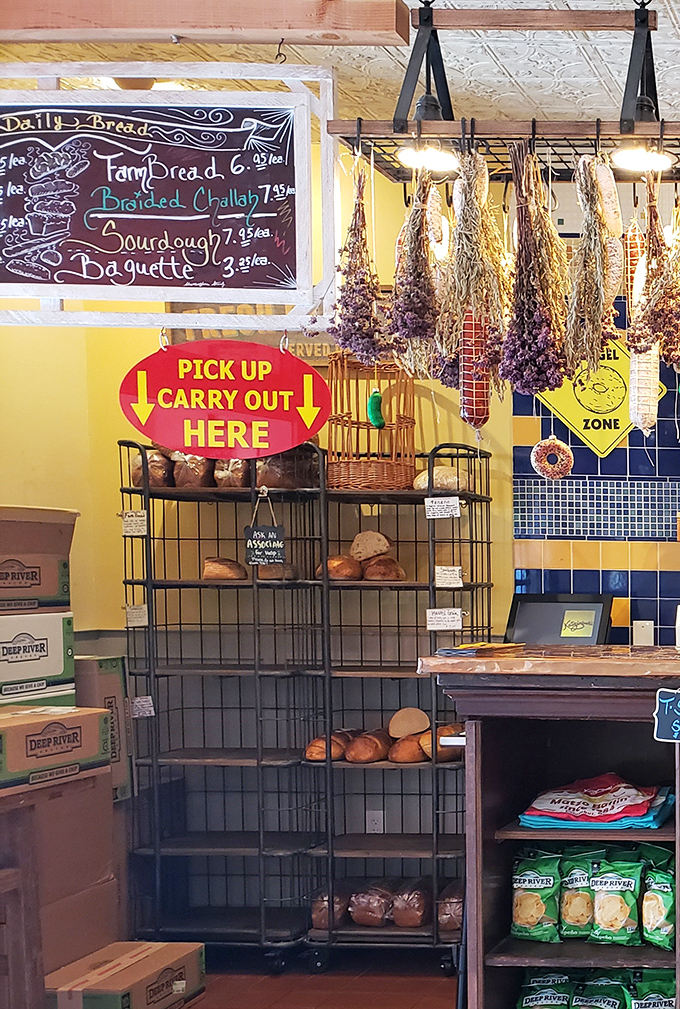 Fresh-baked bread awaits its destiny beneath dried herbs hanging like delicious stalactites. The "Pick Up Carry Out" sign points the way to portable happiness. 