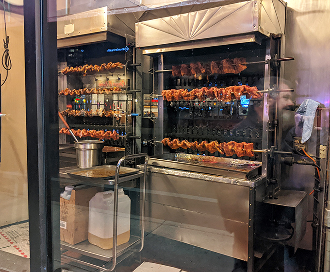 Behind glass, the rotisserie performs its hypnotic dance, transforming ordinary meat into extraordinary barbecue. Meat ballet at its finest.