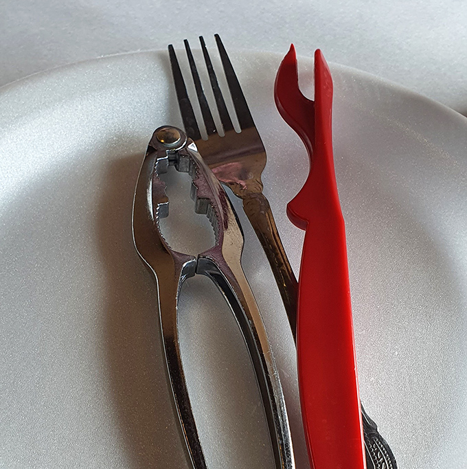 The essential tools of seafood enjoyment—a silver crab cracker and red pick standing ready like specialized surgical instruments for delicious extraction.