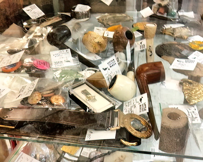 A glass case of curiosities featuring pipes, magnifying glasses, and mysterious objects that belonged in someone's grandfather's desk drawer.