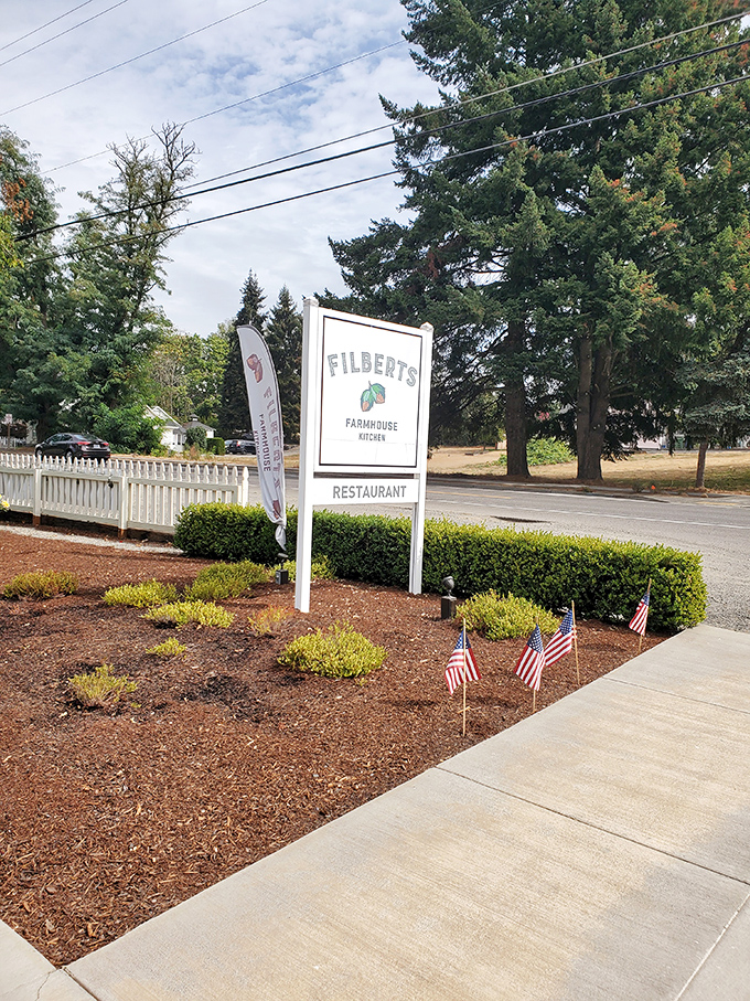 The roadside sign stands like a friendly sentinel, promising culinary delights just beyond those American flags and manicured hedges.