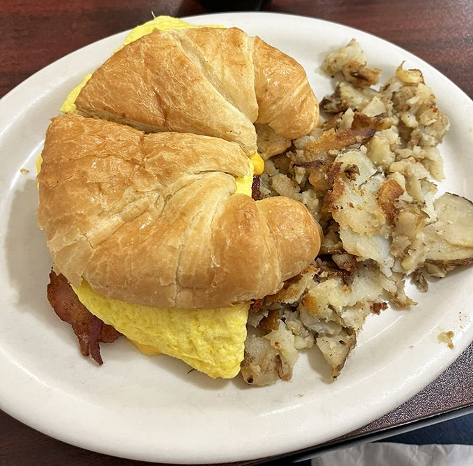 Breakfast sandwich architecture at its finest. Golden croissant, fluffy eggs, and those home fries looking like they're ready for their close-up.