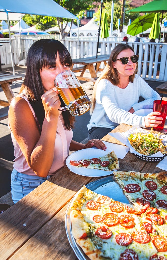 Pizza, beer, and sunshine &ndash; the holy trinity of outdoor dining. These ladies know that happiness is just a slice and sip away.