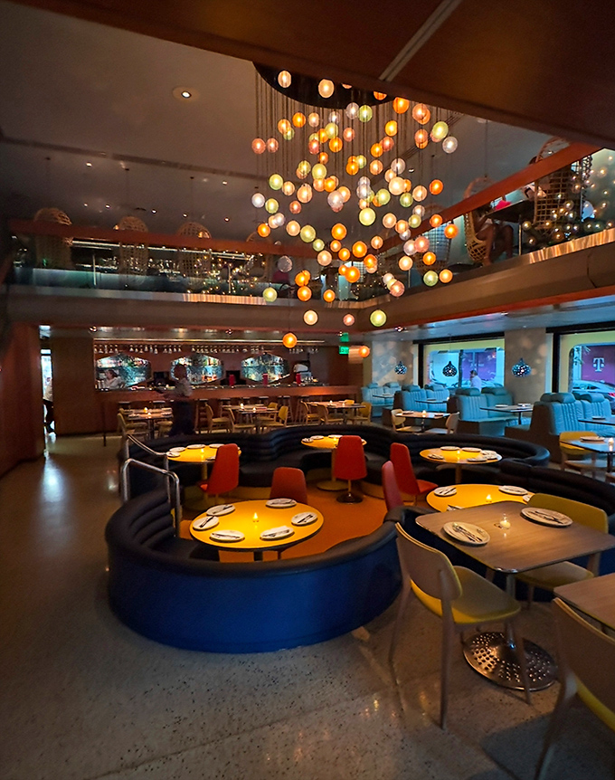 A stunning chandelier of colorful orbs floats above curved banquettes, creating a dining room that feels like a retro-futuristic dream sequence.