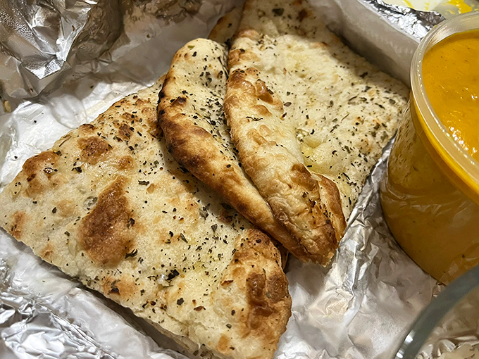 Garlic naan, blistered and buttery, ready to serve as both utensil and indulgence alongside that golden pool of curry.