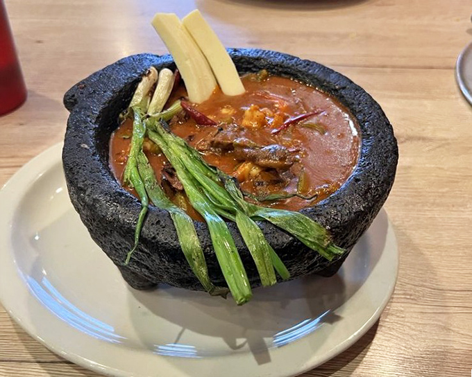 The molcajete arrives like volcanic theater—steam rising from a stone bowl where beef, vegetables, and broth perform a simmering symphony.