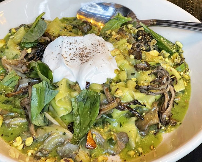 Pasta swimming in a verdant sea of pesto, crowned with a poached egg that's just waiting to create sauce magic. Mushrooms add earthy depth to every bite.