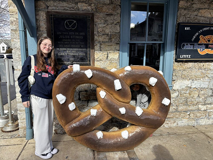 Outside the bakery, a person poses with the giant pretzel sculpture&mdash;creating the ultimate carb-lover's holiday card that relatives will actually want to receive.