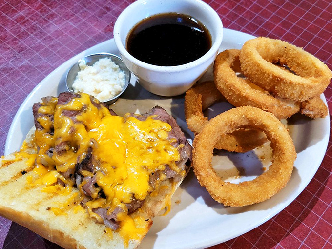 An open-faced prime rib sandwich that's not trying to hide its deliciousness, flanked by onion rings with the perfect crunch-to-tenderness ratio.