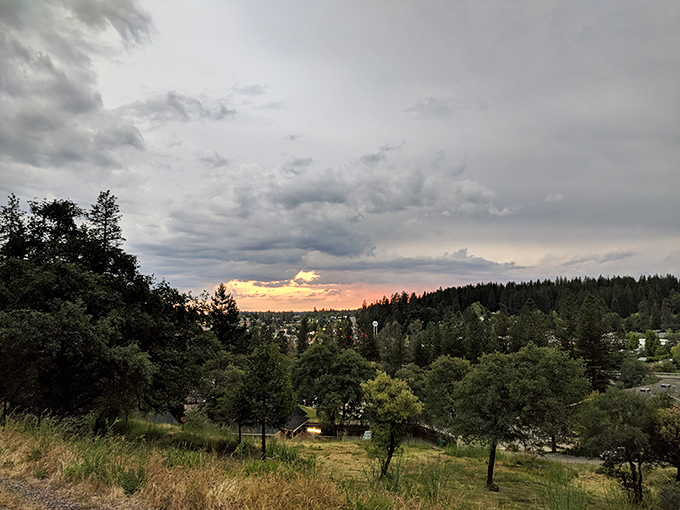 Sunset paints the Sierra sky with dramatic brushstrokes, casting golden light across Nevada City's tree-covered hills and valleys.
