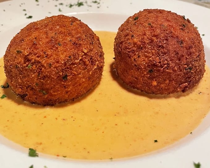 Arancini sitting in a pool of sauce &ndash; crispy, golden orbs hiding creamy risotto centers like delicious little worlds waiting to be discovered.