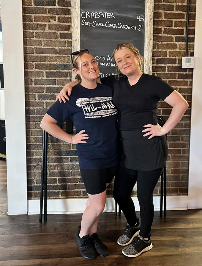 The image shows two staff members standing in front of a chalkboard menu, their friendly smiles suggesting they're ready to guide you through your seafood adventure.