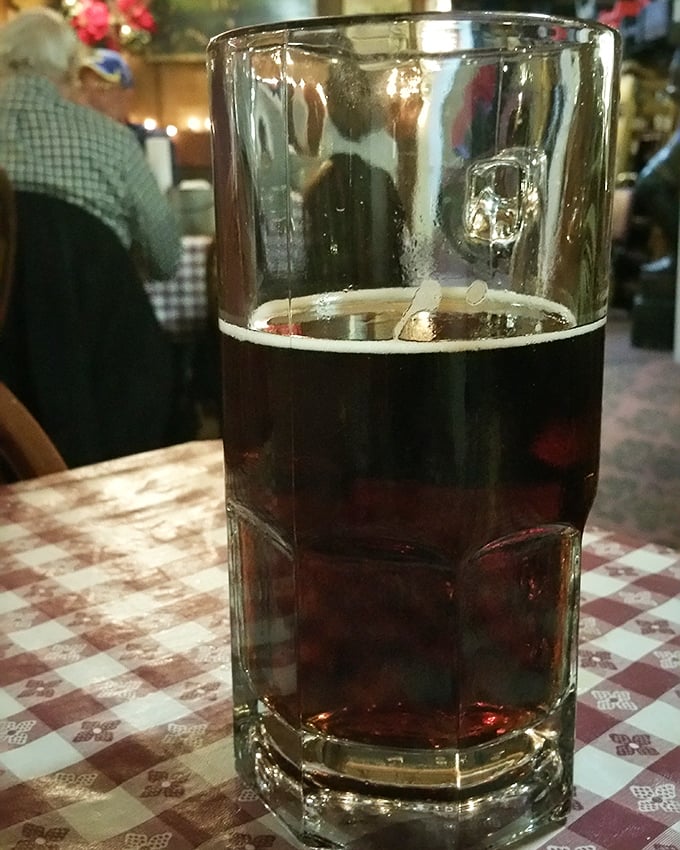 A proper glass of dark beer on a checkered tablecloth &ndash; because sometimes the perfect dining companion doesn't need conversation.