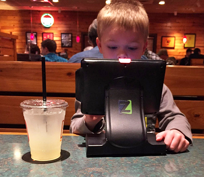 Modern dining meets kid-friendly technology. This little guy's expression says it all: "Food is coming, and I have games. Life is good."