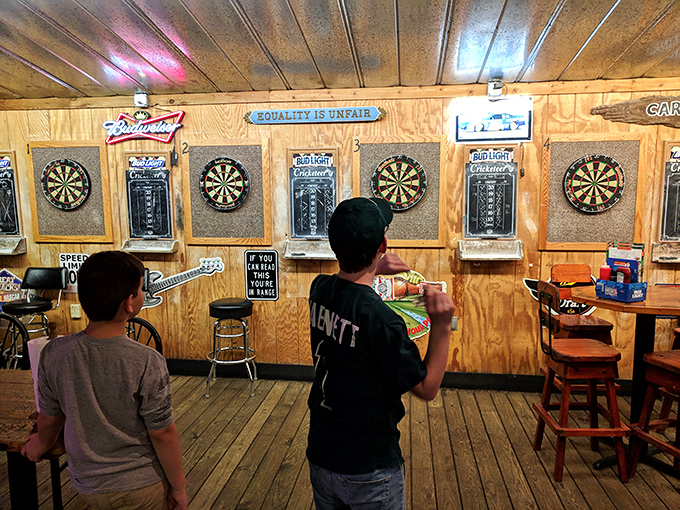 The dart board section: where friendly competitions are born and bragging rights are earned. "Equality is unfair" sign adds to the tavern philosophy.