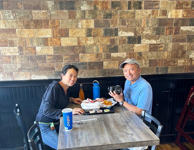 The universal language of good food: two diners sharing a moment of burger-induced happiness against rustic stone walls.