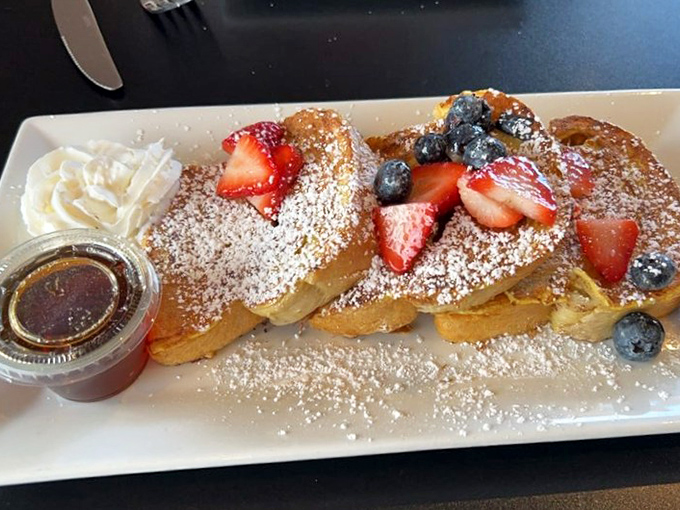 The famous French toast in its natural habitat—powdered sugar snow falling on golden bread islands, with berry inhabitants and a maple syrup lagoon