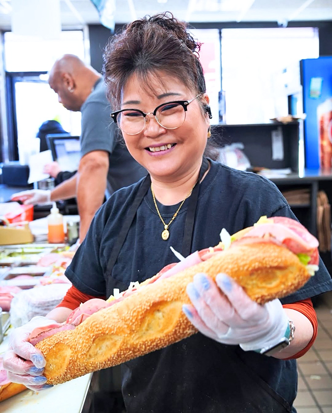 The pride of craftsmanship shines through as this sandwich maker presents her creation. Hoagie happiness personified.