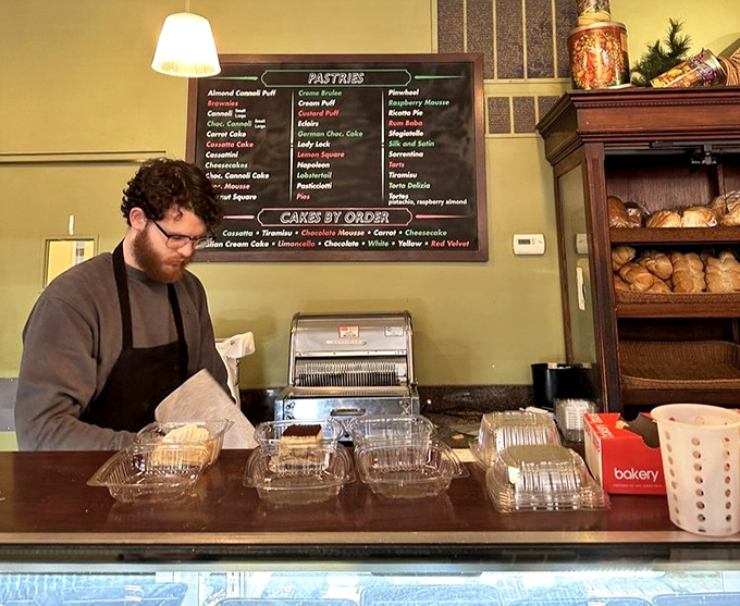 Staff members work with practiced efficiency, wrapping treasures in white boxes. The pastry menu board behind hints at the impossible choices ahead.