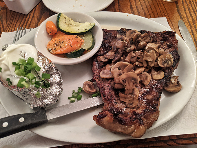 A steak topped with mushrooms that looks like it's auditioning for the cover of "Carnivore Monthly." That baked potato is dressed for success.