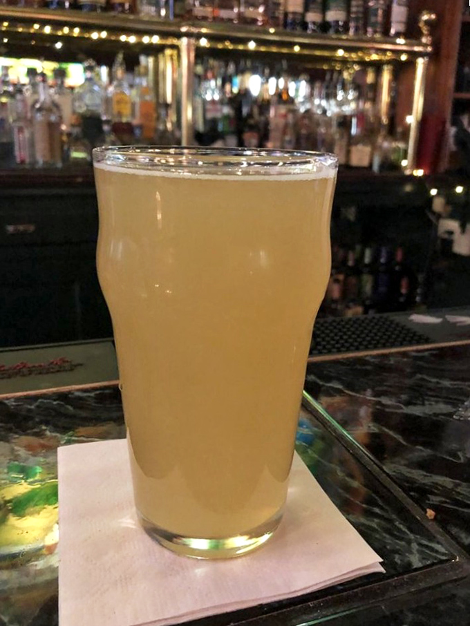 A properly poured pint glowing like liquid sunshine against the bar's backdrop&mdash;proof that sometimes the simplest pleasures are the most profound.