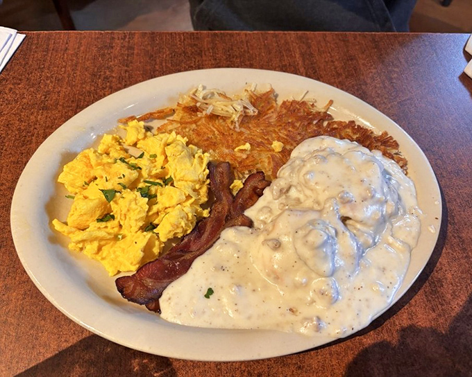 Breakfast's greatest hits on one plate: fluffy scrambled eggs, crispy bacon, golden hash browns, and creamy gravy—the morning equivalent of a perfect playlist.