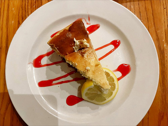 This isn't just cheesecake&mdash;it's a slice of heaven with raspberry drizzle. The lemon wedge isn't decoration; it's essential balance.