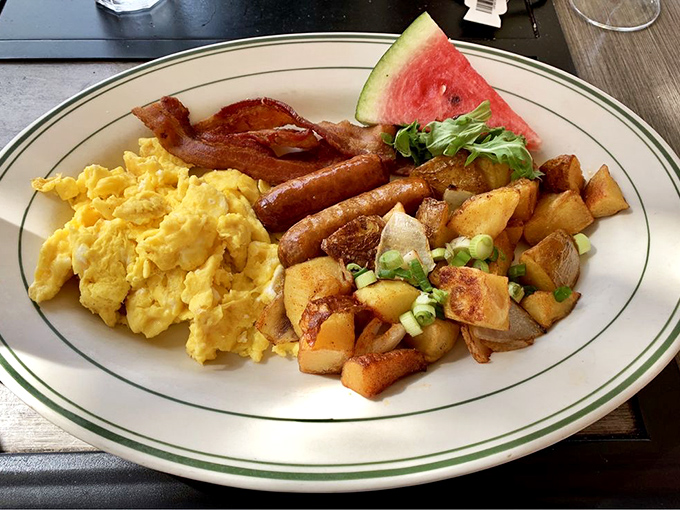 Breakfast perfection on a plate&mdash;scrambled eggs, home fries with green onions, and bacon that means business. That watermelon slice is a thoughtful touch.
