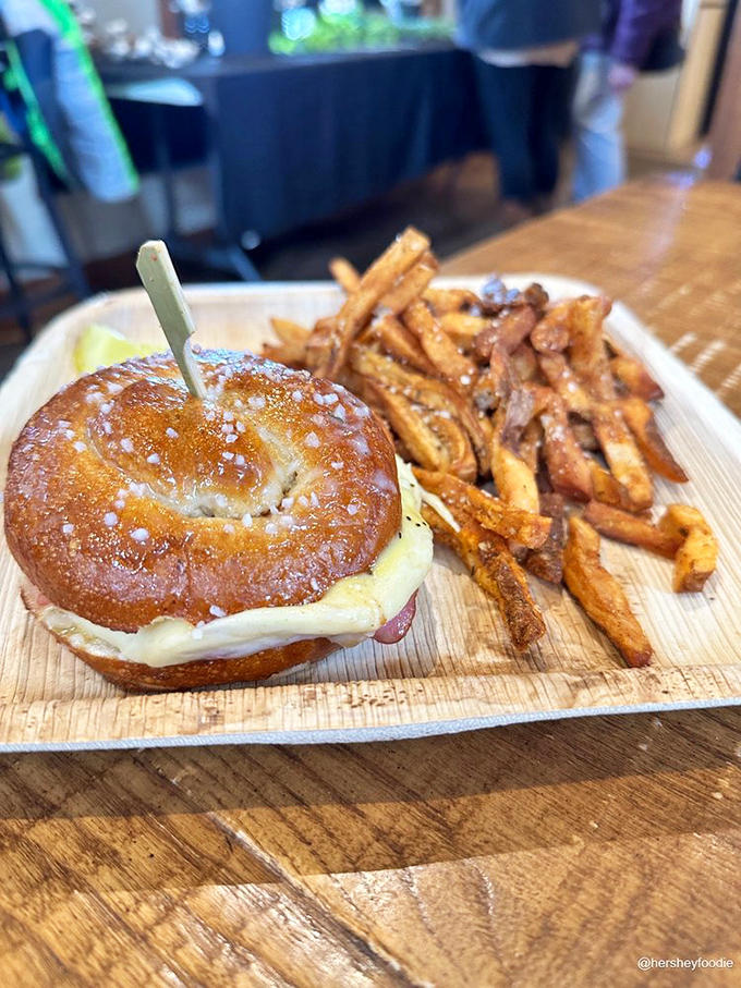 A pretzel sandwich with sweet potato fries that makes you question why you ever settled for lesser lunches. Pure comfort on a wooden board.