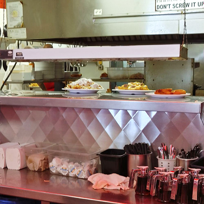 Behind the pass, where diner magic happens – plates waiting for pickup under heat lamps tell stories of hash browns crisped to perfection and eggs cooked just right.