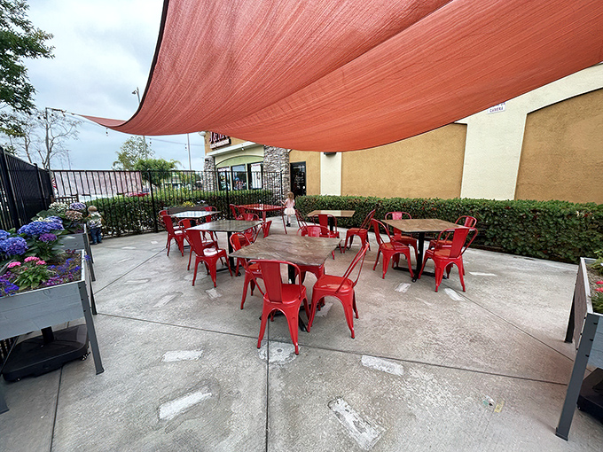 The outdoor patio offers al fresco dining under a coral canopy, where bright red chairs pop against the concrete like exclamation points in a delicious conversation.