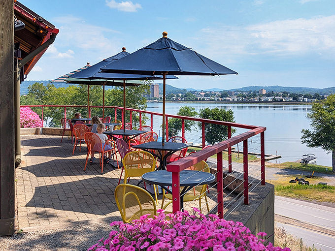 The colorful patio chairs pop against the river backdrop, creating an outdoor dining space that feels like a backyard party with better food.