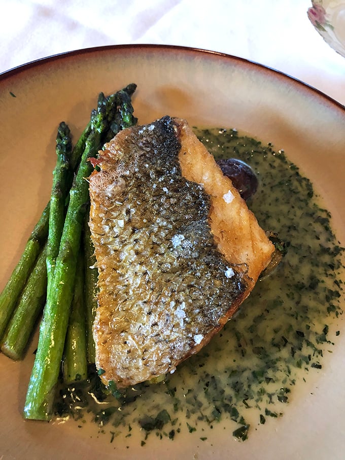 Sea bass that practically leaps off the plate, accompanied by asparagus standing at attention. The herb-flecked sauce pools around it like a delicious moat protecting a culinary castle.