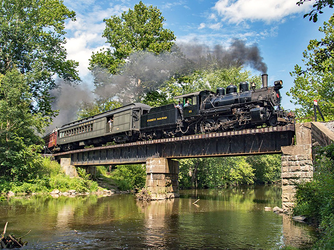 The locomotive crosses the stone bridge, creating a perfect harmony of industrial might and natural beauty that photographers dream about.