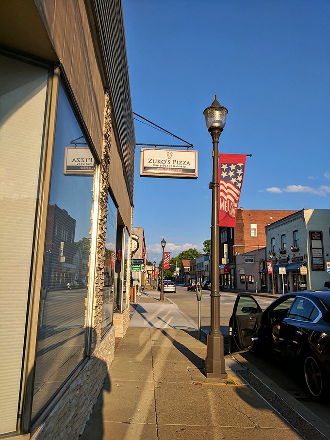 Zuko's Pizza sign hangs alongside patriotic banners on a street where the evening light makes even ordinary sidewalks look like movie sets.