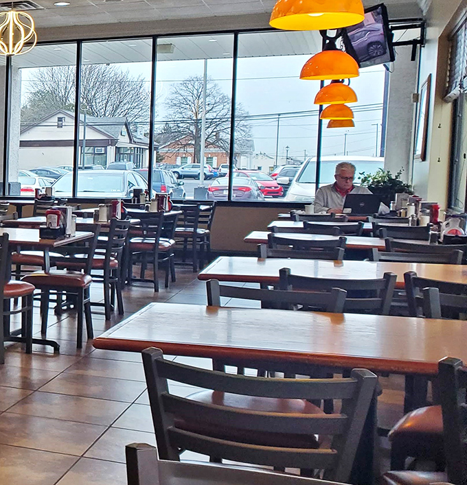 Orange pendant lights hang like morning suns above tables where solo diners find peaceful refuge with newspapers and pancakes.