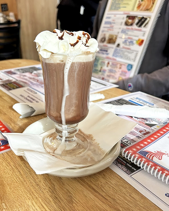 Hot chocolate that's wearing its Sunday best. That whipped cream isn't just a topping—it's a cloud of happiness with chocolate drizzle racing down the sides.