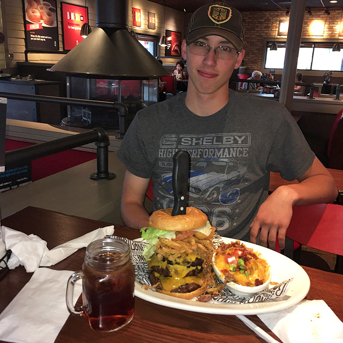 The face of satisfaction alongside a burger that requires engineering skills to eat. Some meals are worth the structural challenge.