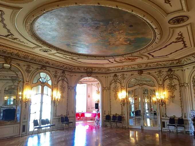 This elegant salon looks ready for a Bridgerton ball. The painted ceiling, gilded details, and crystal sconces create an atmosphere of refined luxury.