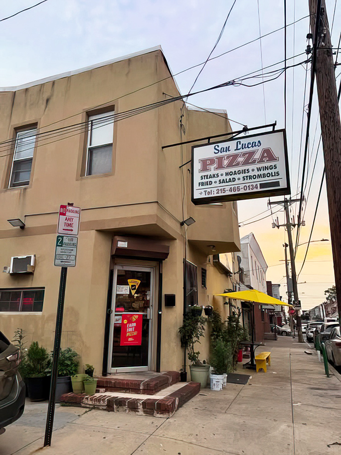 The yellow umbrella and potted plants add a touch of charm to this corner pizzeria. Urban dining with neighborhood character.