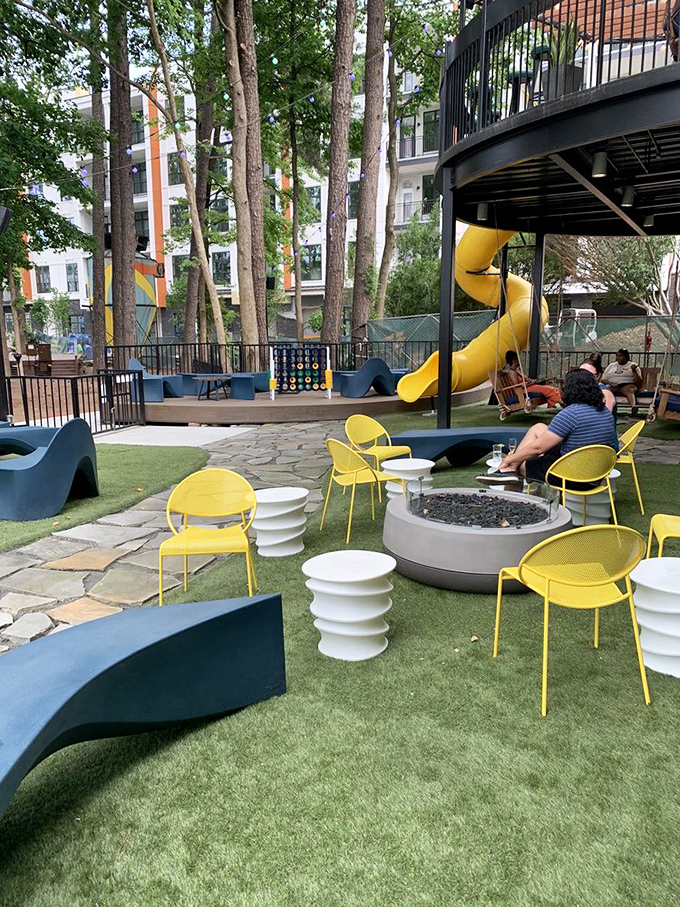 The outdoor area combines playground elements with sophisticated lounging. Yellow chairs pop against artificial turf, creating an adult recess you never want to end.