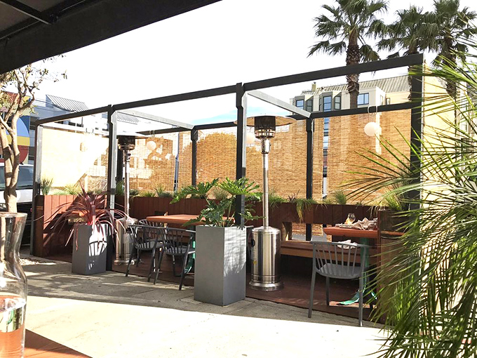 The outdoor seating area offers an urban oasis for enjoying maritime delicacies. Palm fronds and bamboo screens create a microclimate of calm amid city energy.