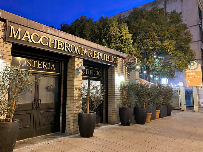 As night falls, Maccheroni Republic transforms into a beacon of pasta possibility, its golden sign promising comfort in carbohydrate form.