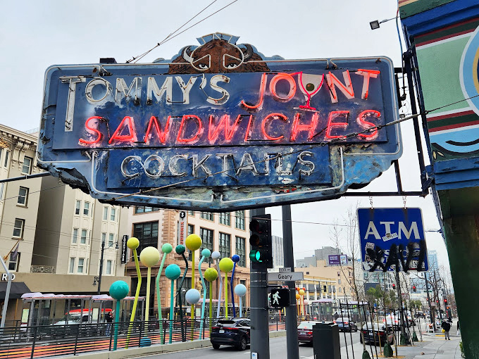 The neon sign cuts through San Francisco fog like a beacon, promising sandwiches and cocktails to weary urban travelers since long before you had a smartphone.
