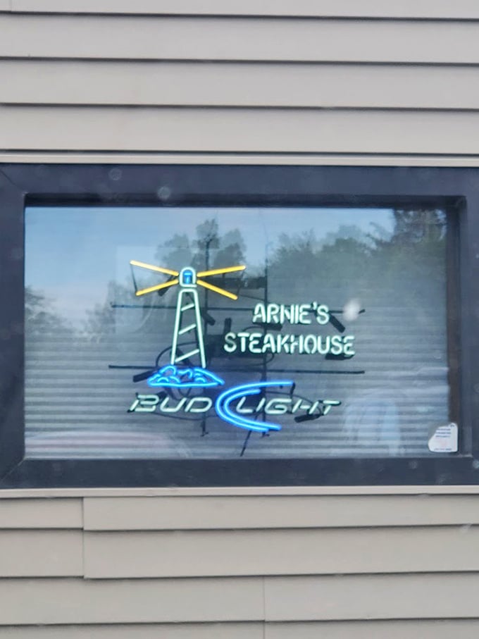 The neon lighthouse in the window signals safe harbor for the hungry. Like a beacon to seafood and steak lovers navigating dinner decisions.