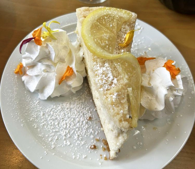 A slice of lemon cheesecake so divine it should come with a warning label. Those edible flowers aren't just pretty—they're a promise of excellence.