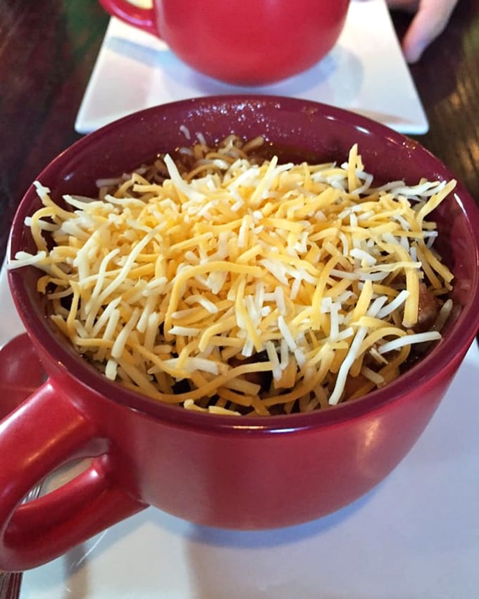 A bowl of chili topped with enough cheese to make Wisconsin proud. This isn't just lunch&mdash;it's a warm hug on a cold day, served in a cheerful red mug.