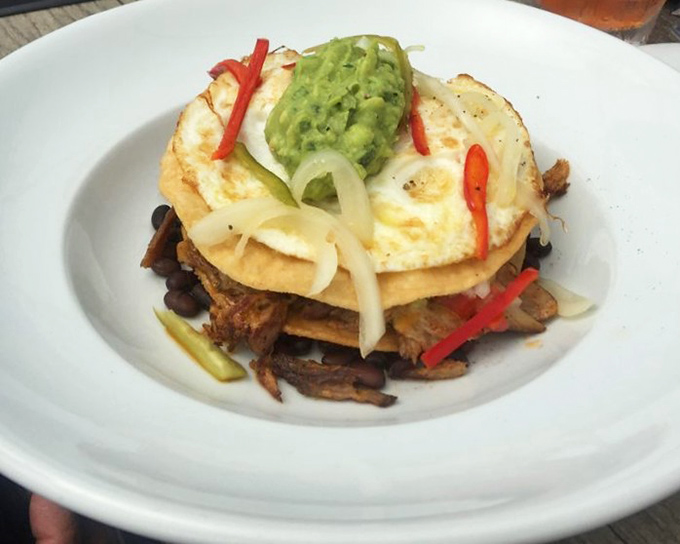 Breakfast that doesn't know it's breakfast: crispy tortillas, savory meat, and a sunny-side-up egg crowned with avocado. Morning glory on a plate.