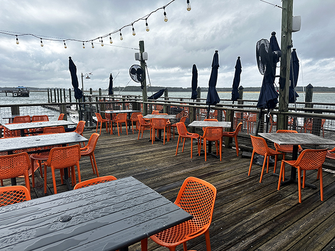Orange chairs pop against weathered wood decking, creating the perfect perch for waterfront dining. Even on cloudy days, this view delivers sunshine.
